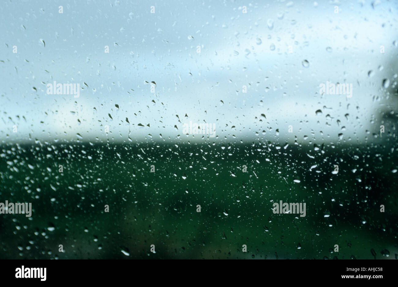 Drops of rain on outside of window with half green half grey background ...