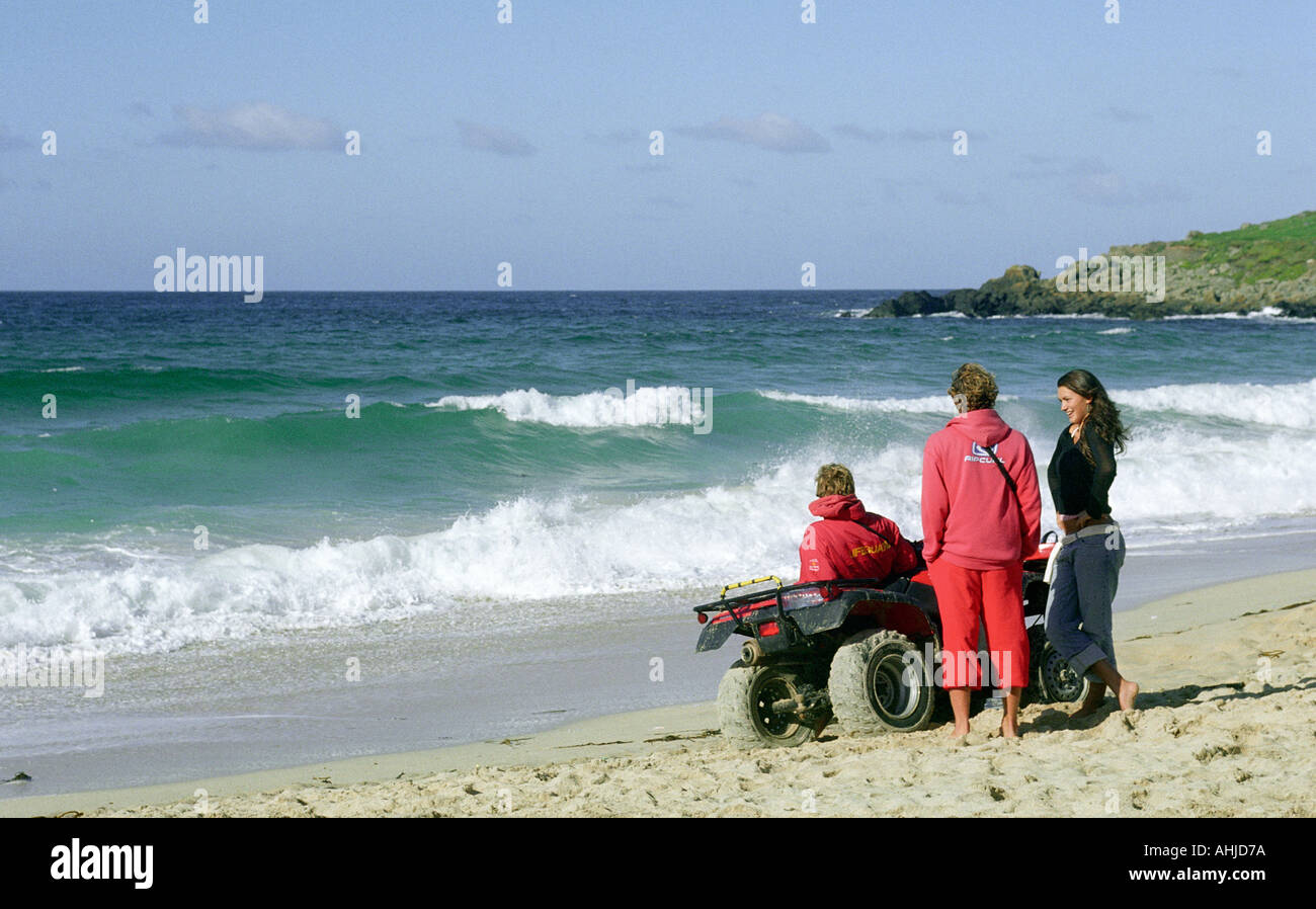 Lifeguard in red uniform standing by quad bike with another lifeguard ...