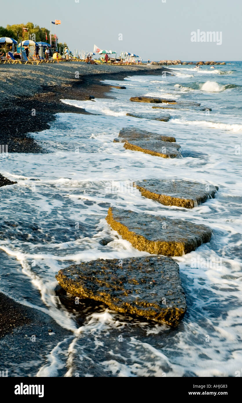 Rock stone path and black stone sand beach and people swimming in ...