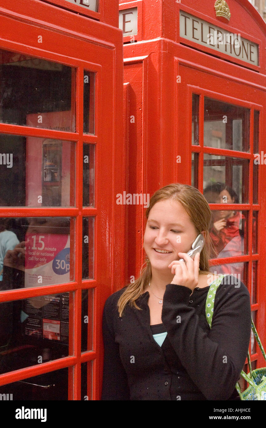 Teenager using cell phone in front of traditional red phone booths in ...
