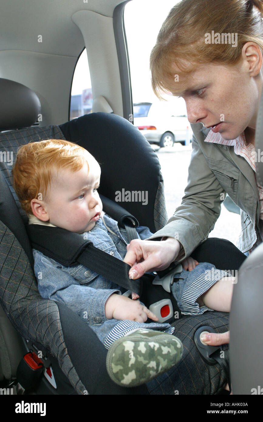 A mother ensuring her baby is correctly strapped in to a childs car ...