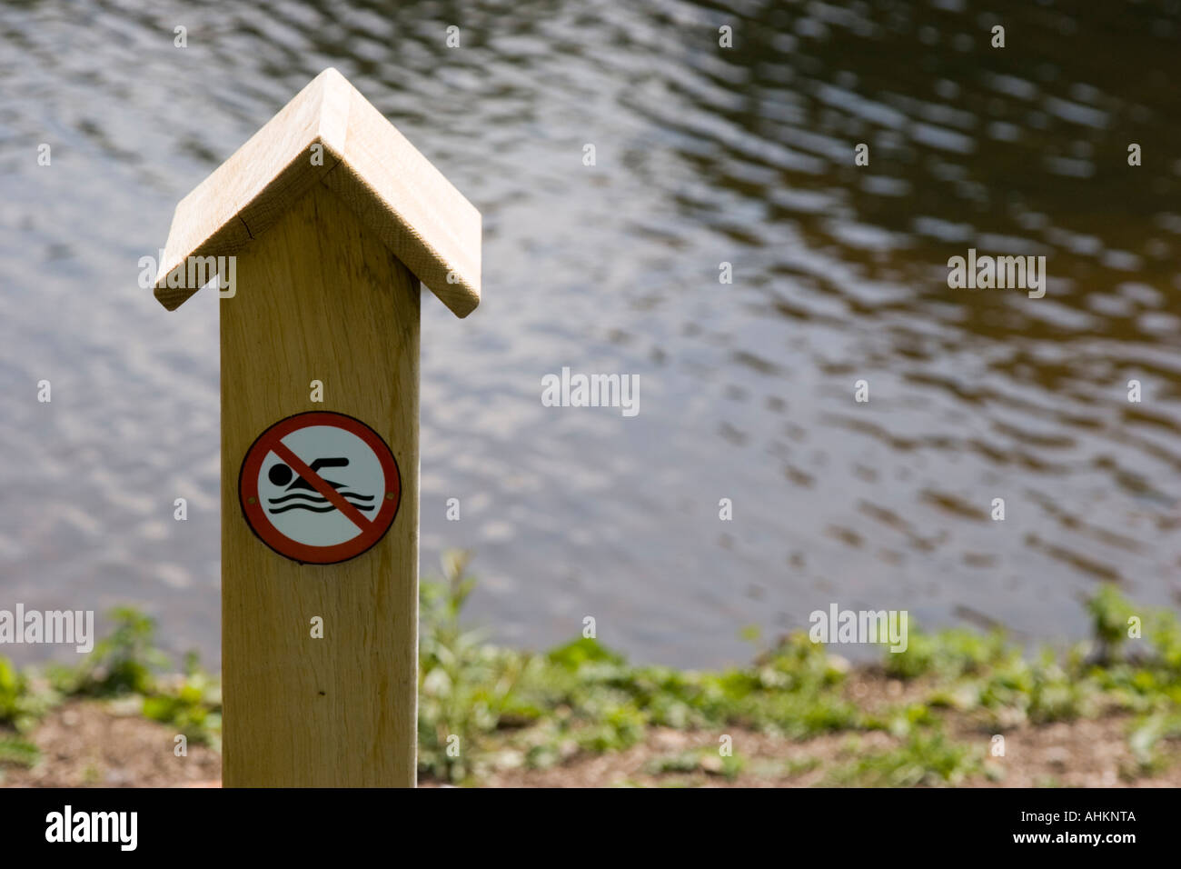 Wooden post showing no swimming sign next to a lake Stock Photo - Alamy