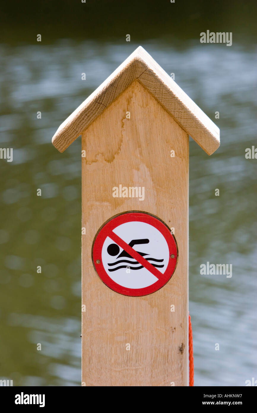 Wooden post showing no swimming sign next to a lake Stock Photo - Alamy