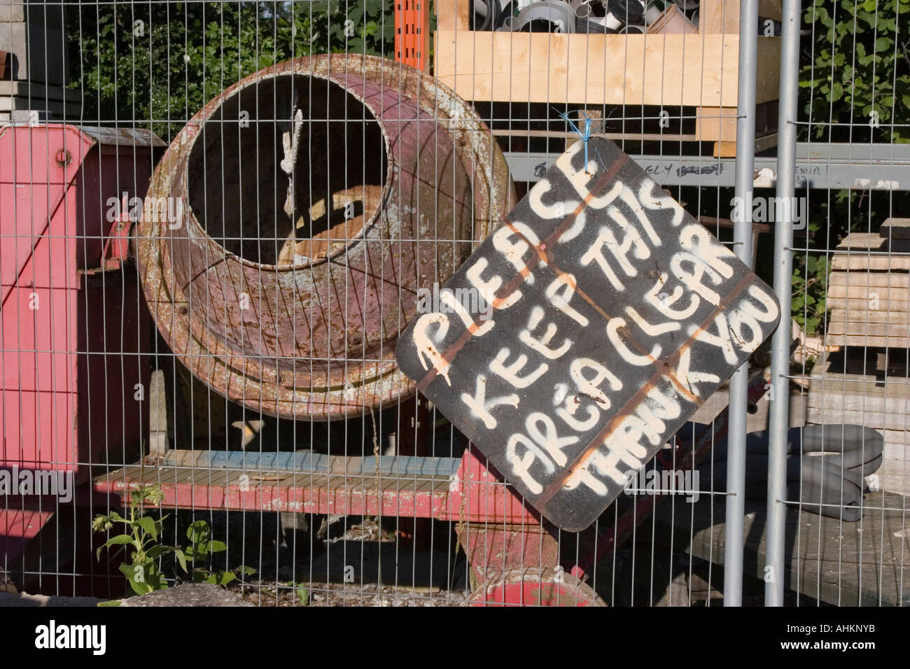 Clutter around an old cement mixer with sign saying Please keep this ...