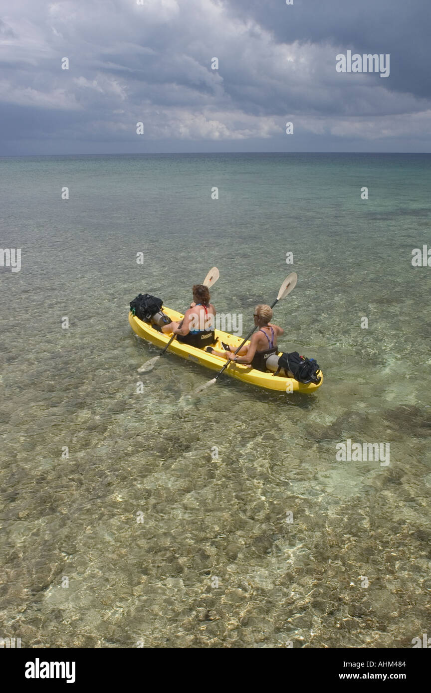 Two women with dive equipment paddling a kayak over a shallow reef in ...