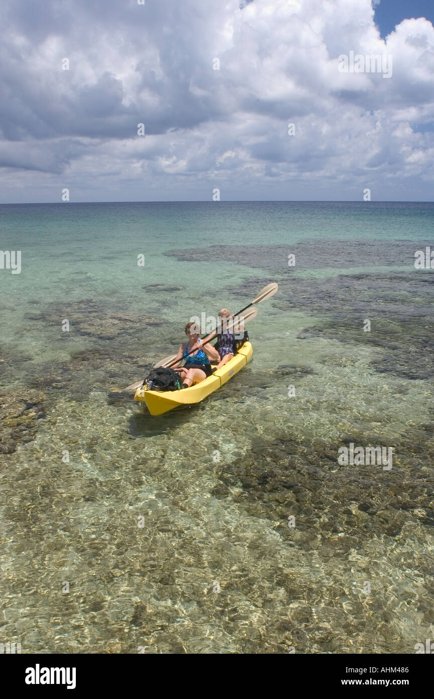 Two women with dive equipment paddling a kayak over a shallow reef in ...