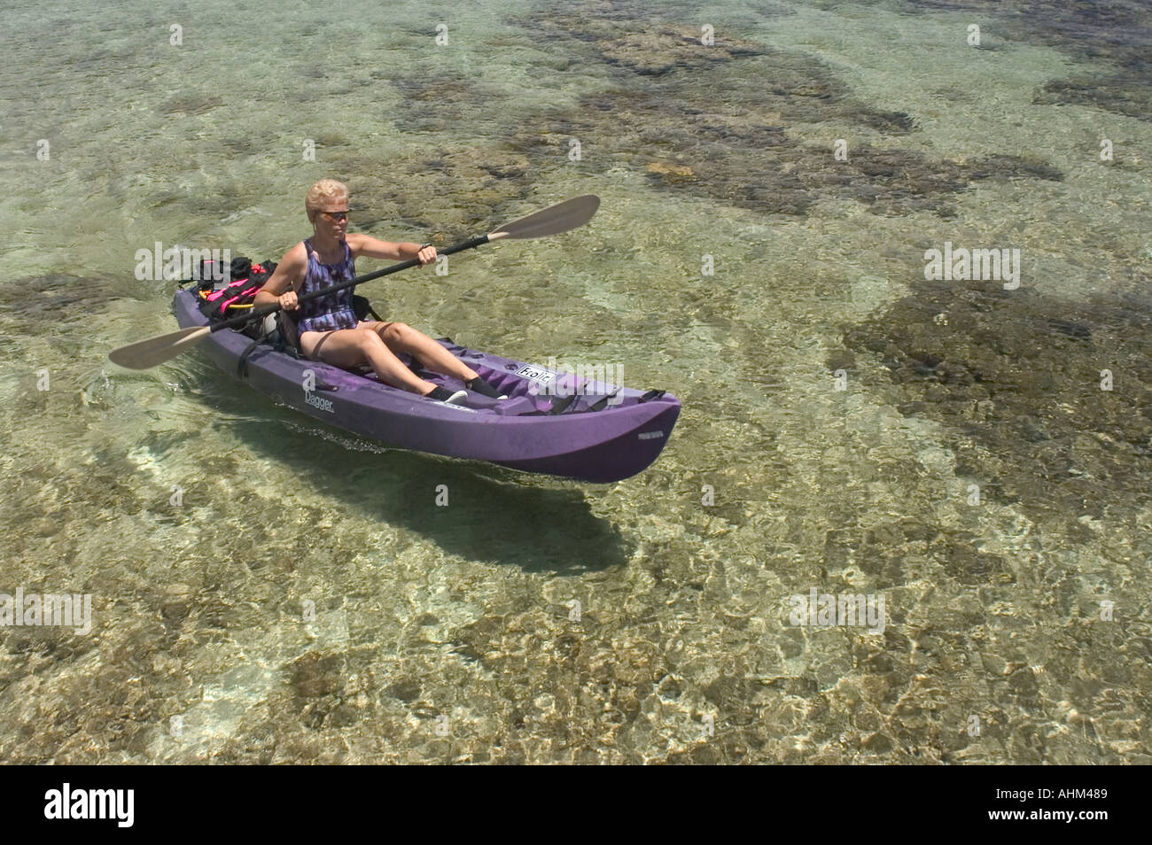 Woman with scuba diving equipment paddling a kayak over a shallow reef ...