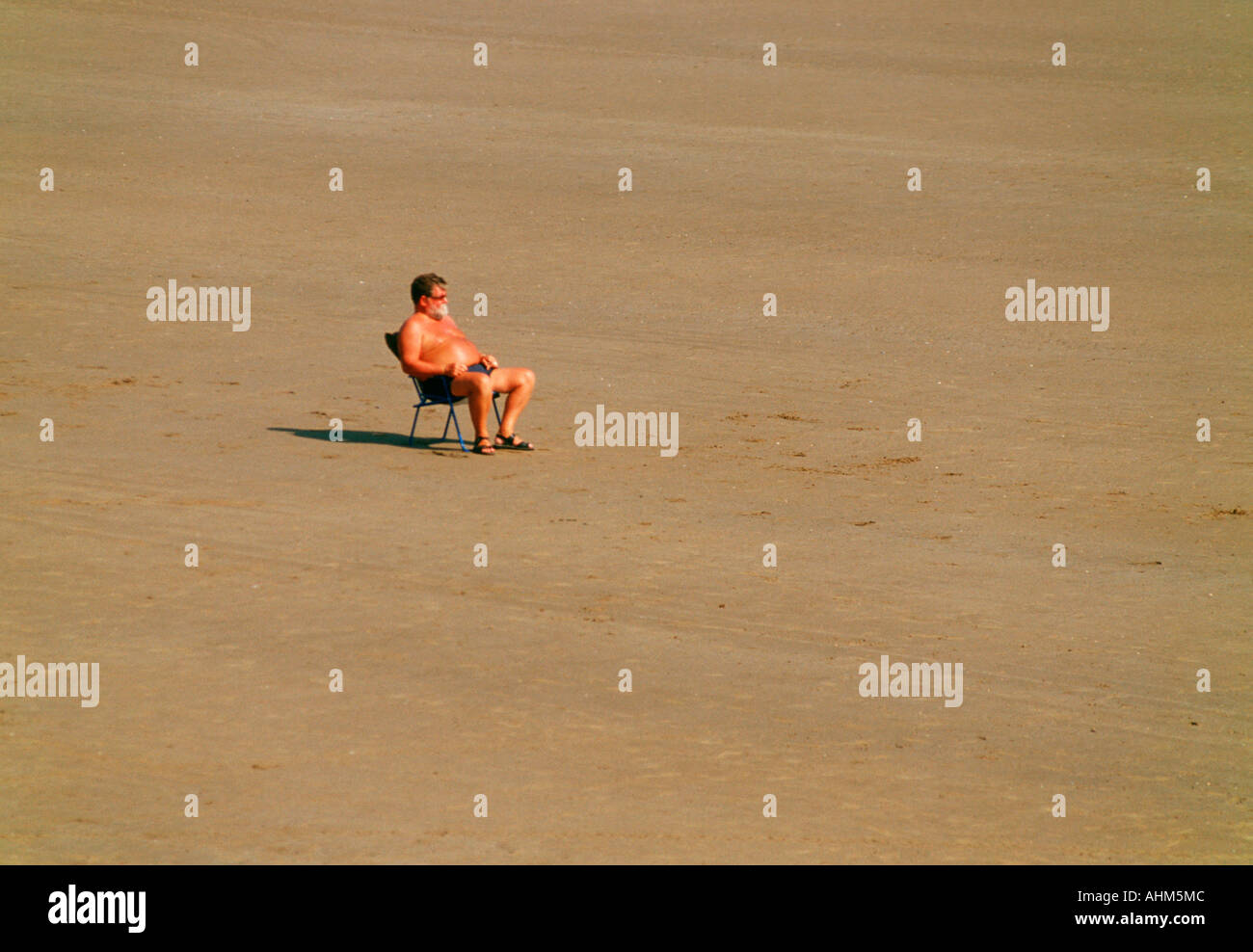 A man sitting in a deck chair on a completely deserted beach at Filey ...