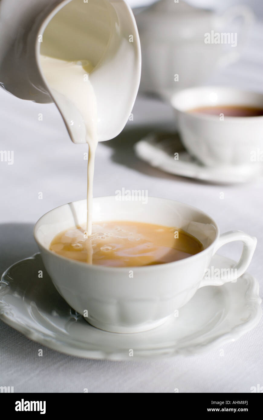 Pouring milk from porcelain milk jug into cup filled with tea Stock ...