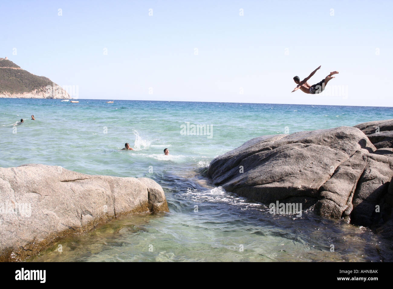 Young men diving from rock on beach at Solanas Sardinia Italy ...