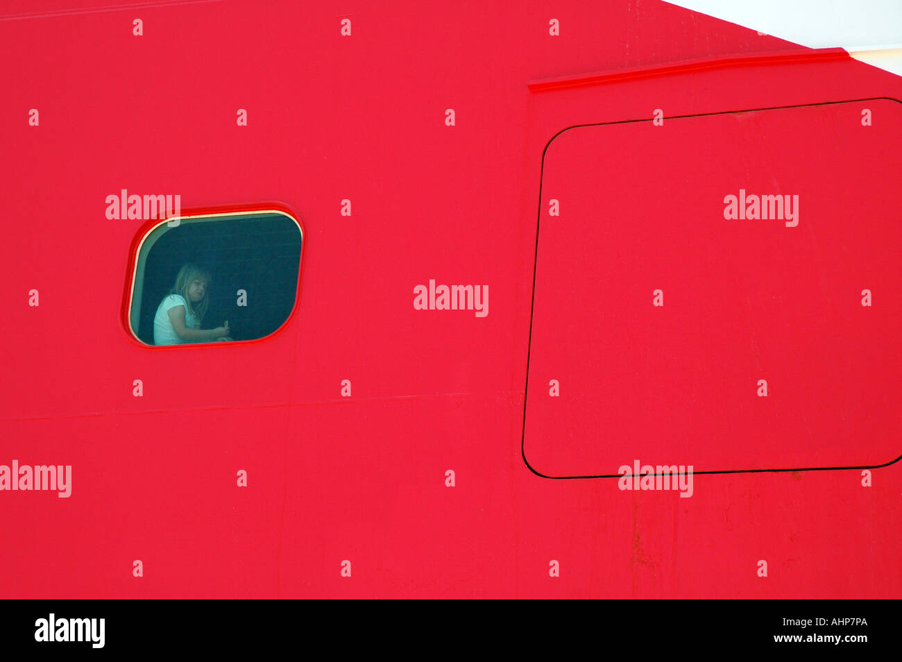 Young girl looking out from a porthole at the side of a cruise liner ...