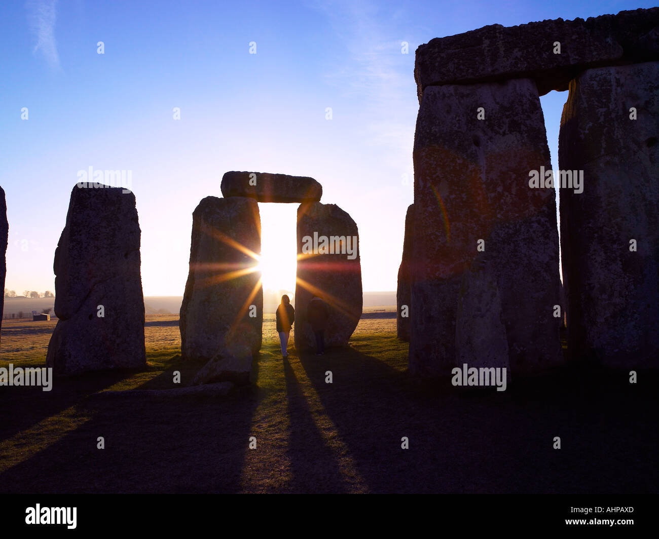 Sun shining through the stones at Stonehenge with a person standing by ...