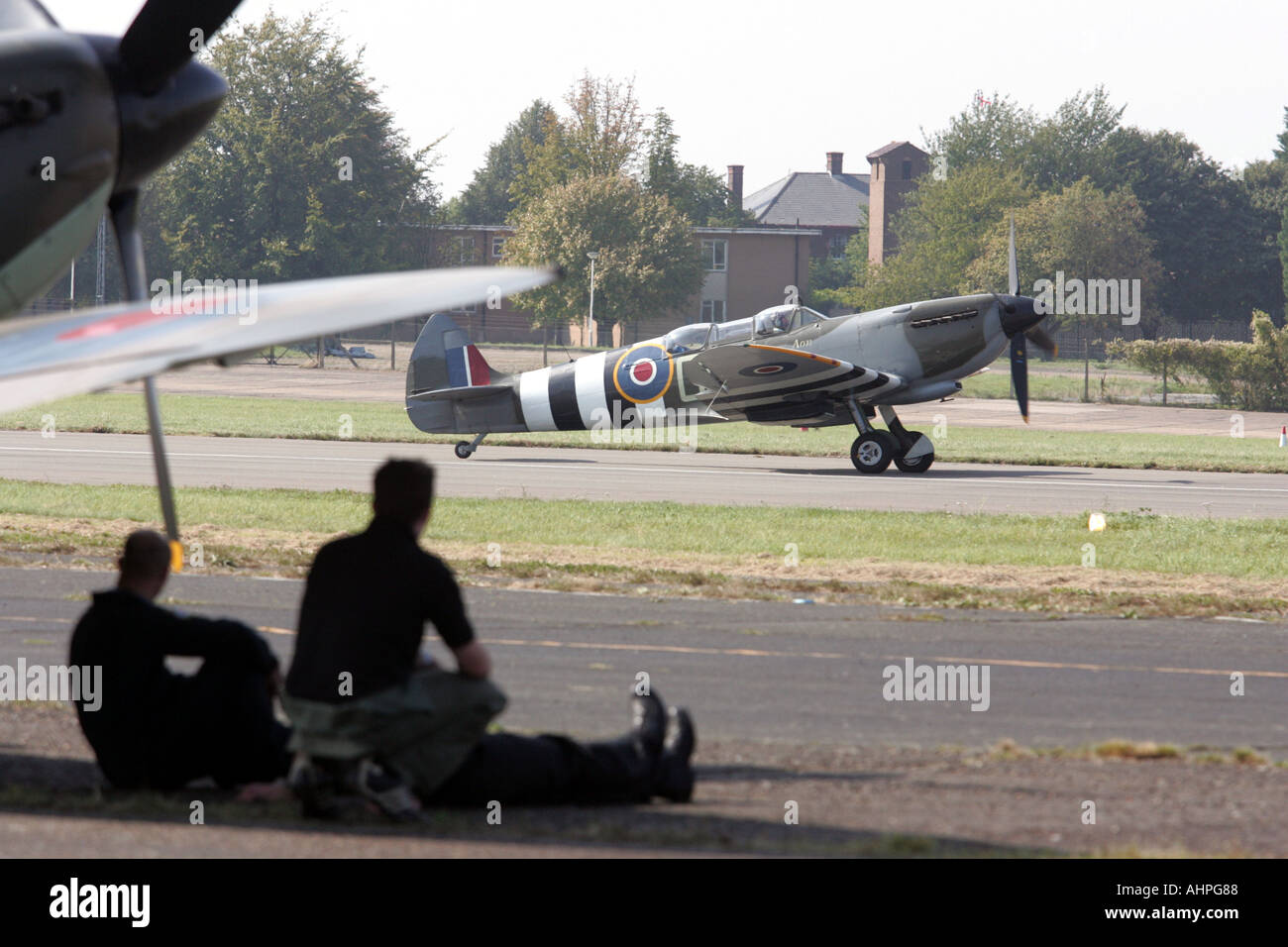 Engineers in the shadow of a spitfire wing watch a Spitfire take off ...