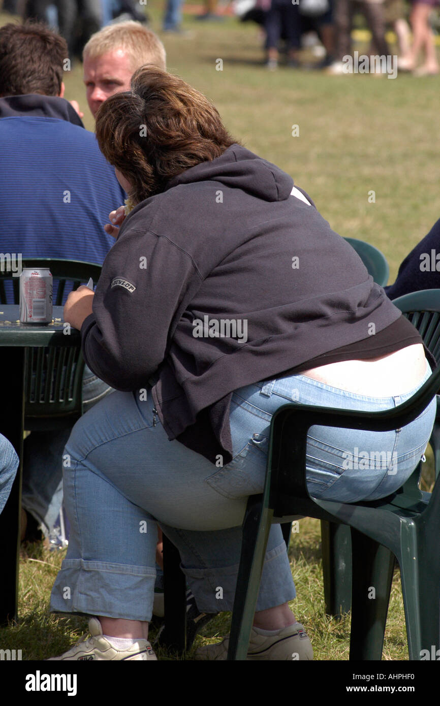 Fat woman sitting in a plastic chair eating a hotdog and burger at an ...