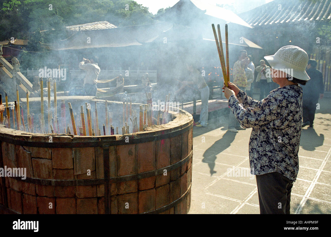 Asian woman praying with josticks at a temple in Kunming Yunan Province ...