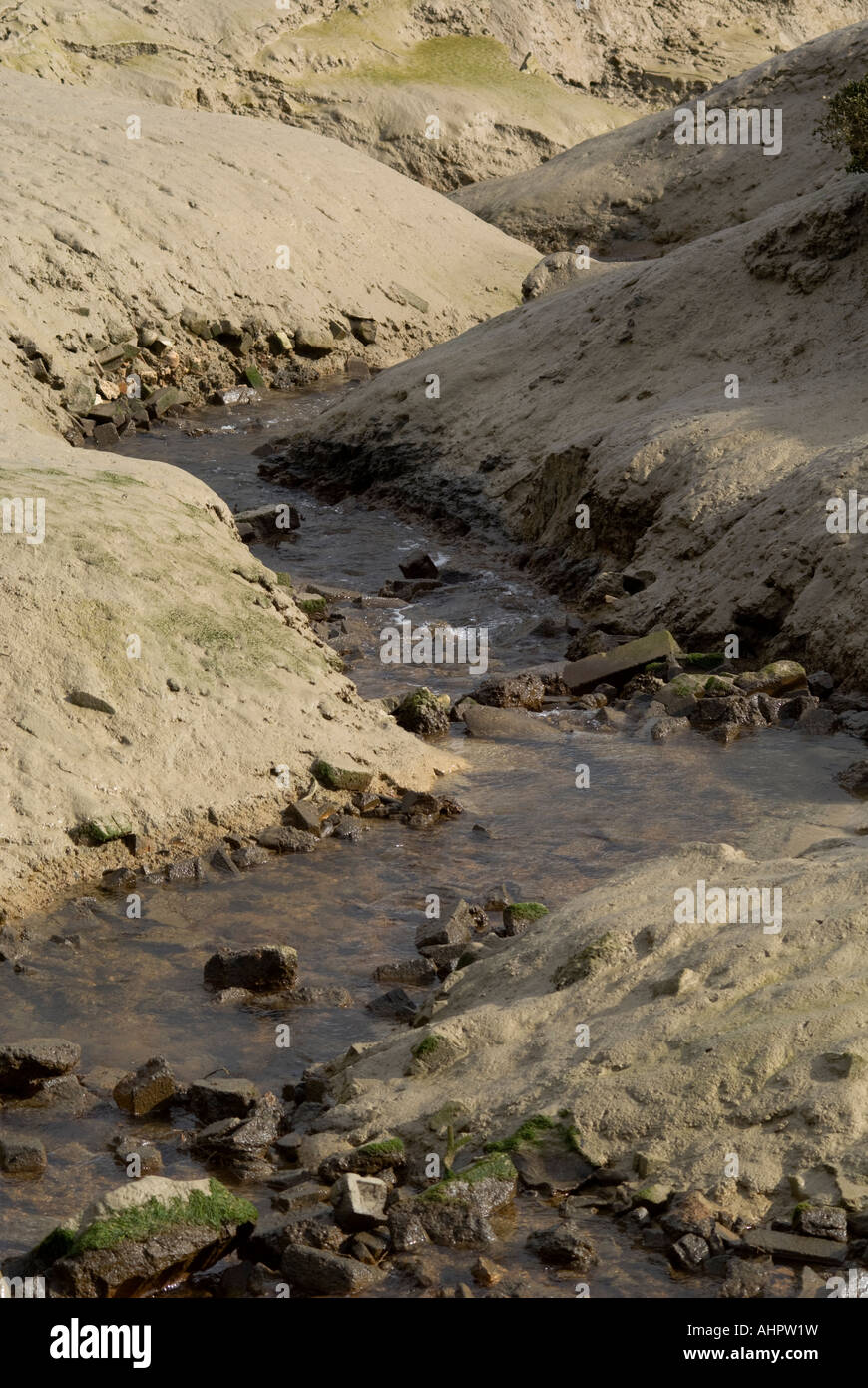 A water channel running into a river with mud banks on either side ...