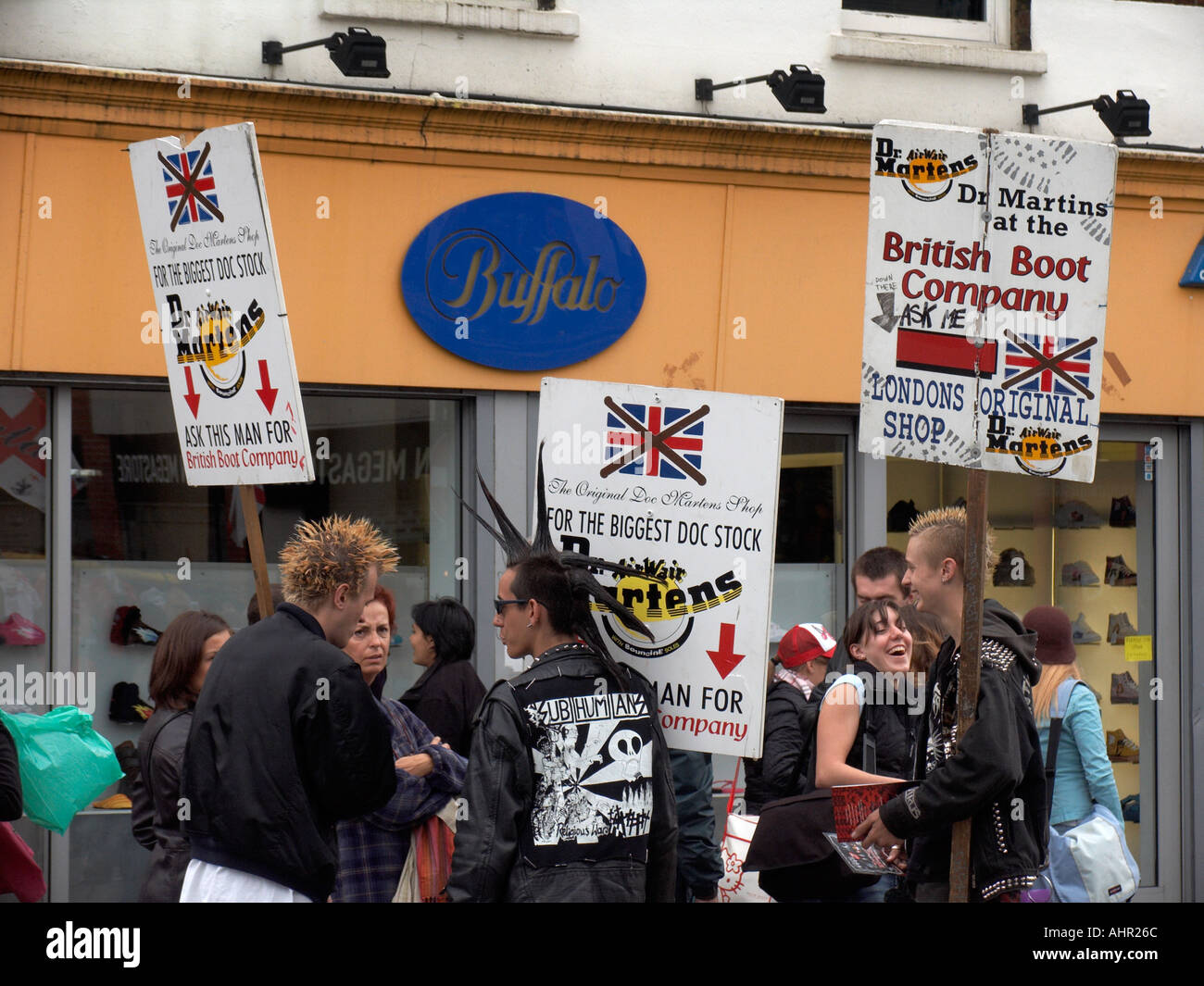 Punk dressed men with sign boards advertising on sidewalk Camden High ...