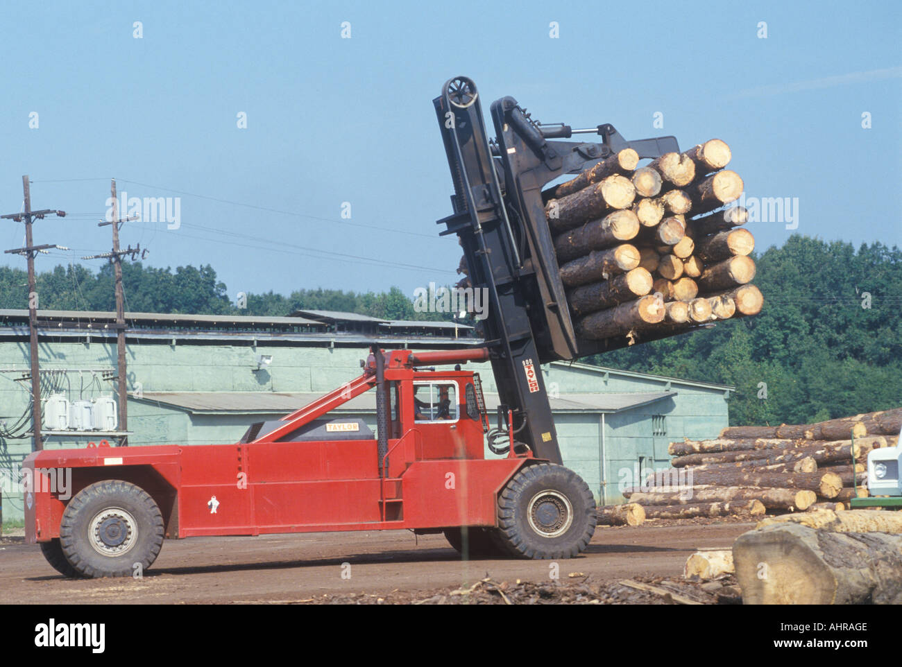 An industrial forklift moving a large bundle of logs at a container ...