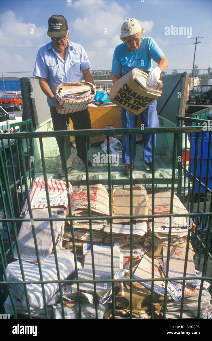 A couple throwing newspaper bundles into a bin to be recycled at the ...