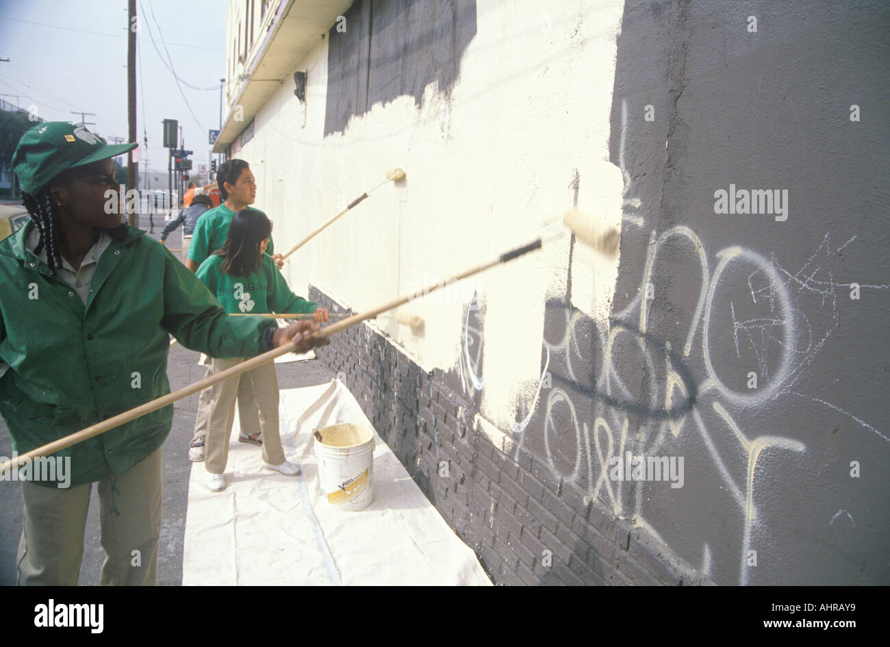 A group of kids repainting the side of a building defaced by graffiti ...