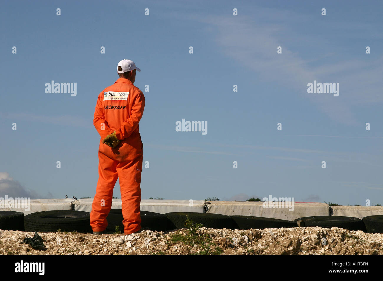 Track racing marshall in orange protective overall at side of race ...