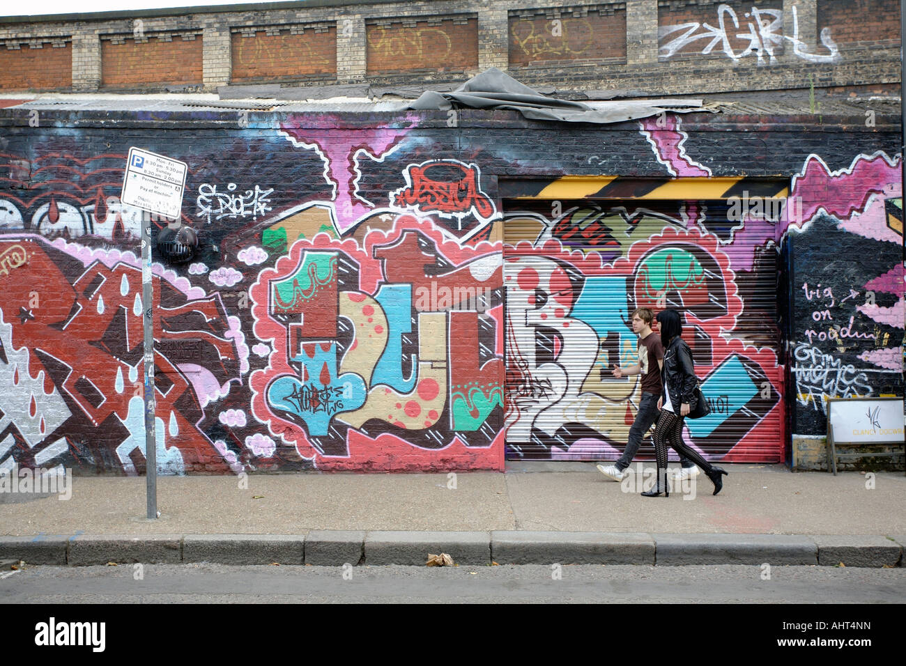 Couple walking past graffiti. Sclater Street, Shoreditch, Tower Hamlets ...