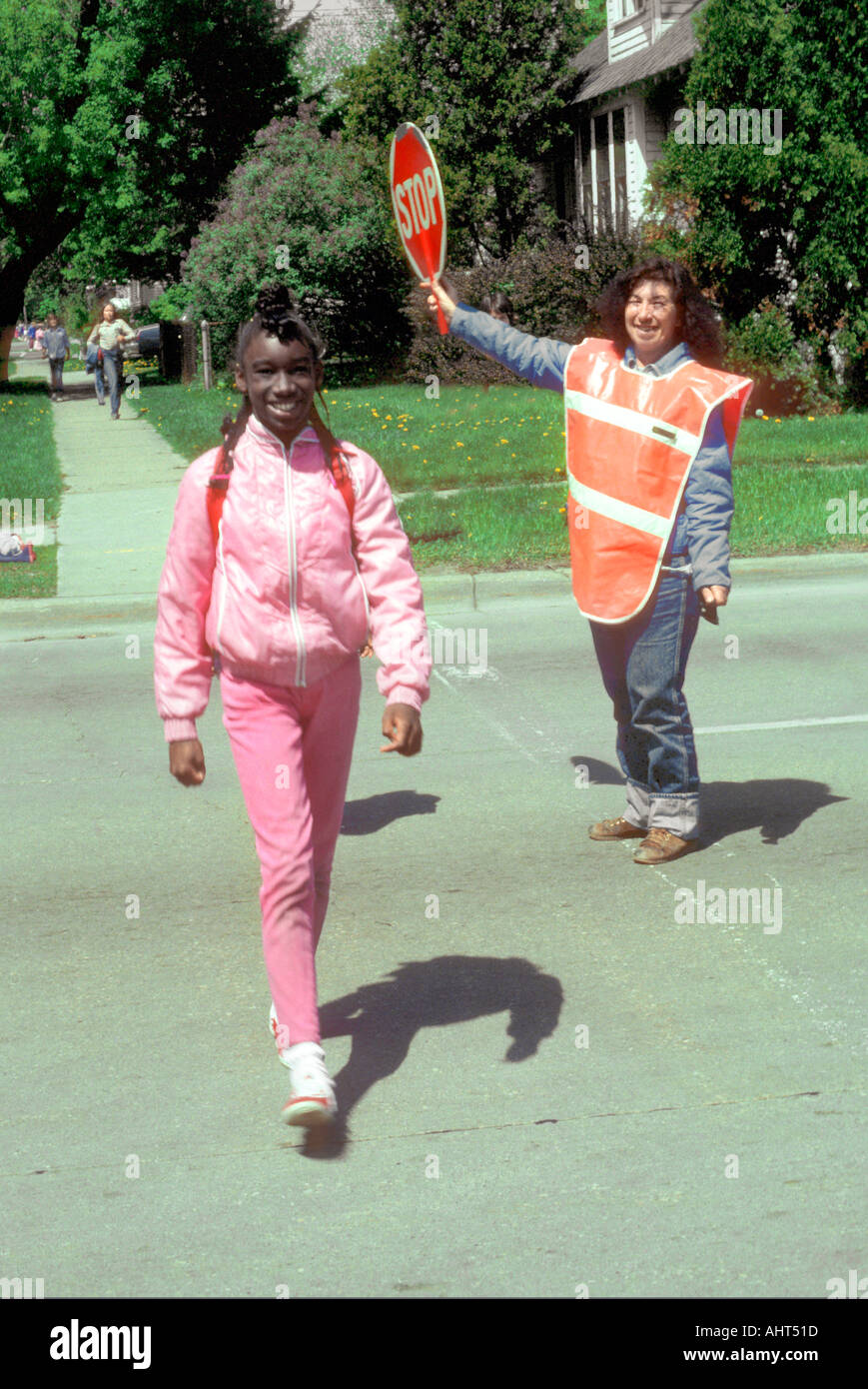 Adult crossing guard allows safe passage for black female to cross a ...