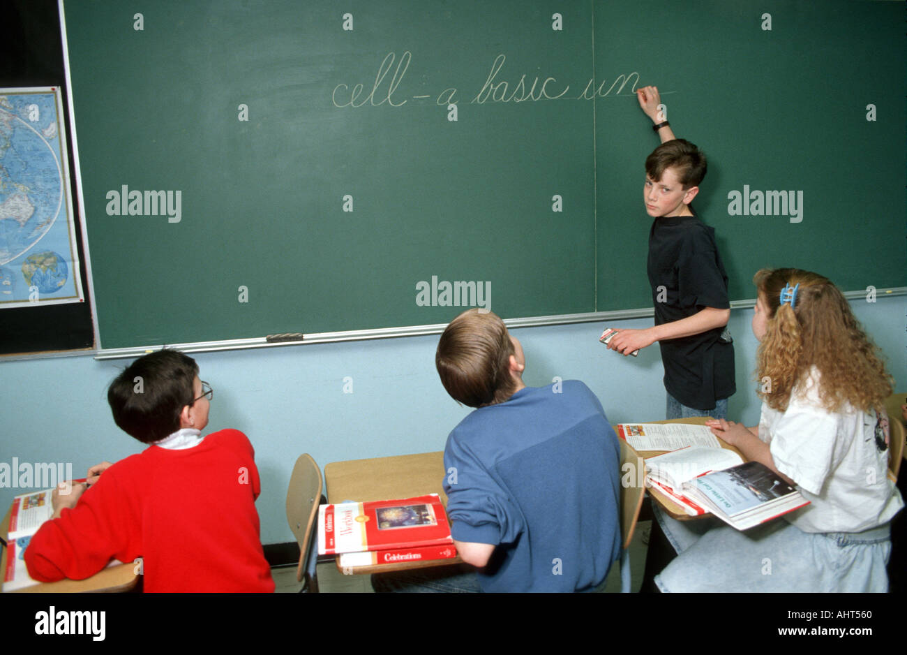 Middle school student writes word definition on board class looks on ...
