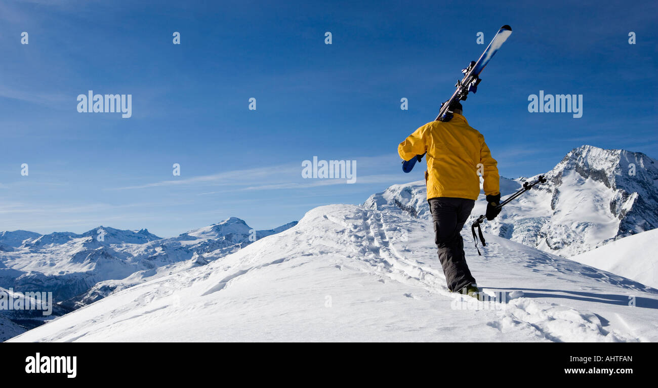 Male skier walking over mountain ridge carrying skis, rear view Stock ...