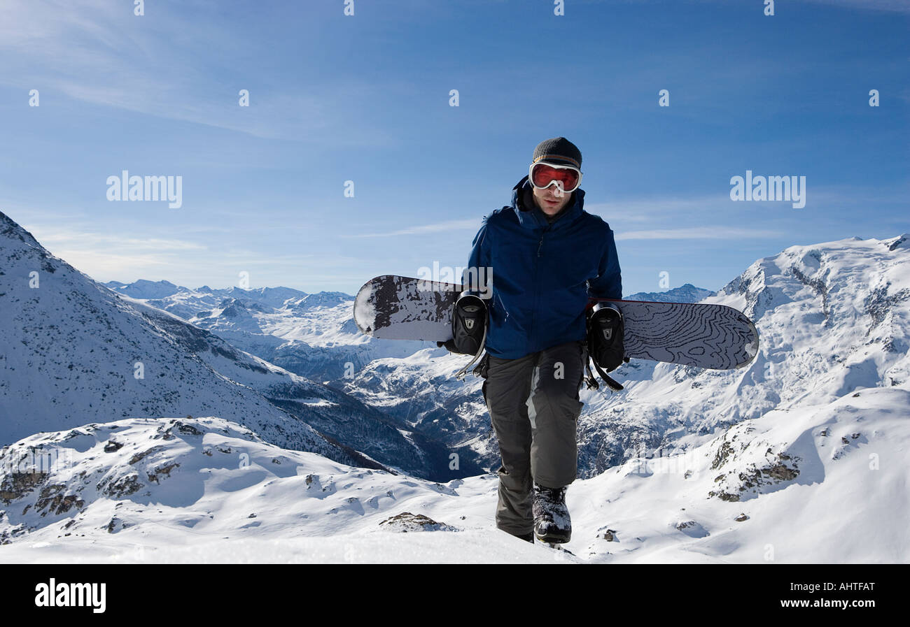 Male snowboarder walking up mountain ridge carrying snowboard Stock ...