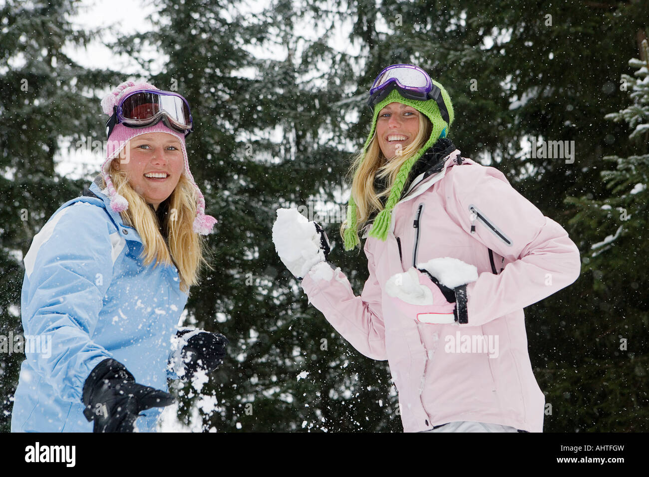 Two young blonde women wearing ski-wear throwing snowballs at camera in ...