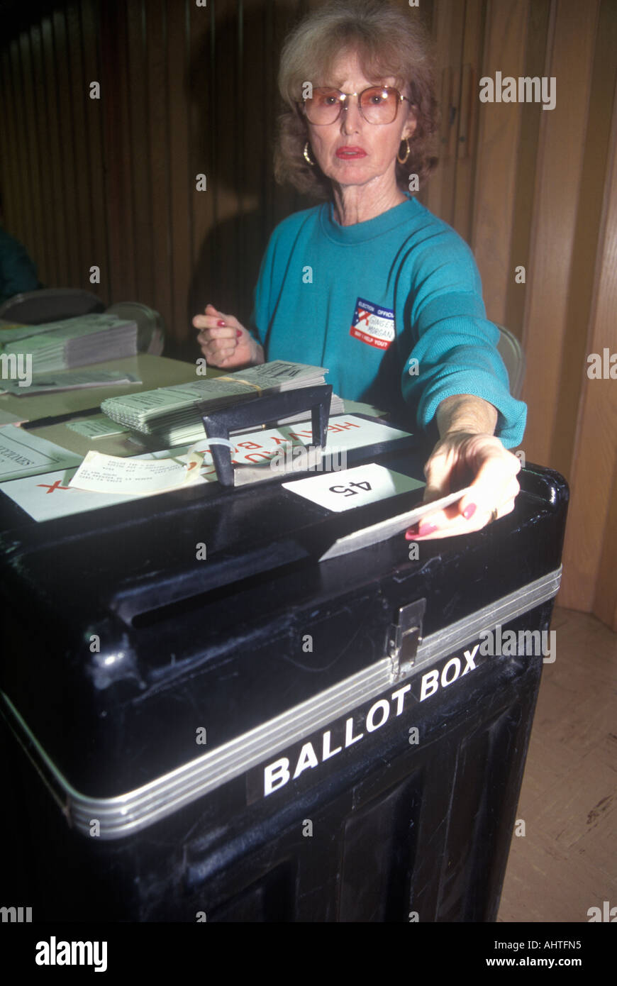Election volunteer depositing ballots in a ballot box in a polling ...
