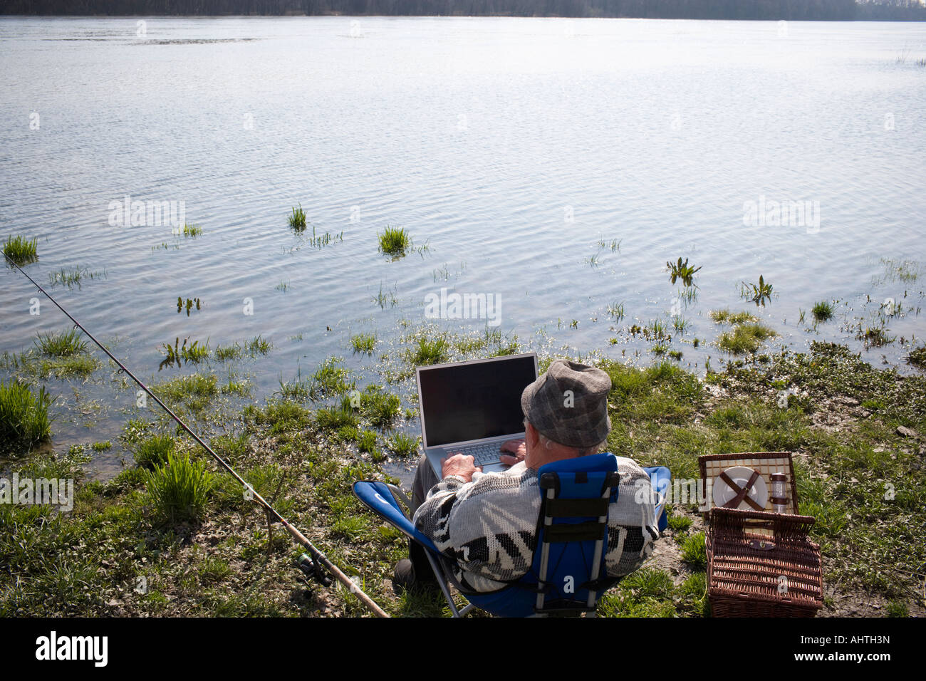 Senior man fishing by river, using laptop, rear view Stock Photo - Alamy