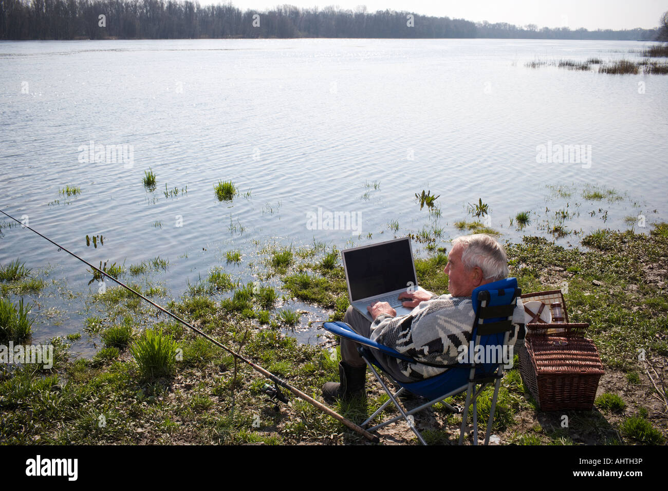 Senior man fishing by river, using laptop, rear view Stock Photo - Alamy