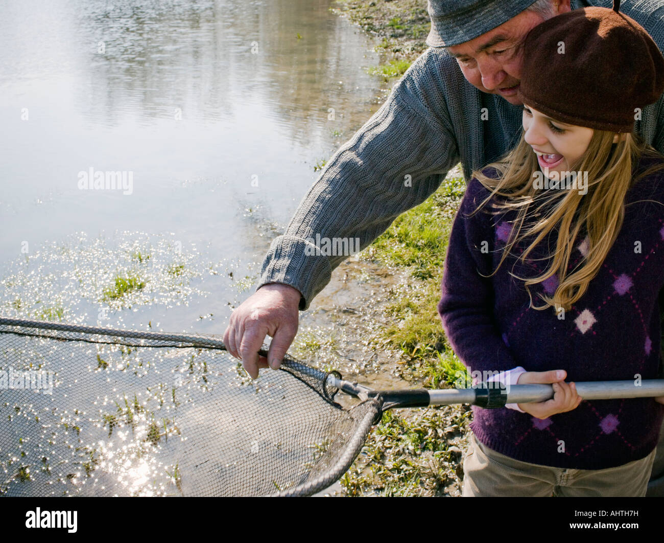 Grandfather helping granddaughter (10-12) use fishing net by river ...
