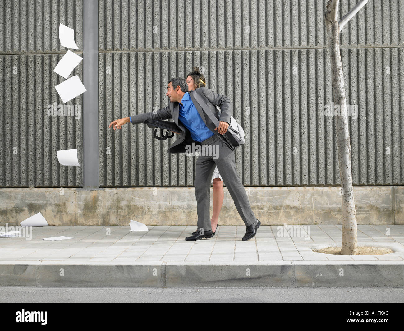 Older man and young woman chasing papers blown by the wind down the ...