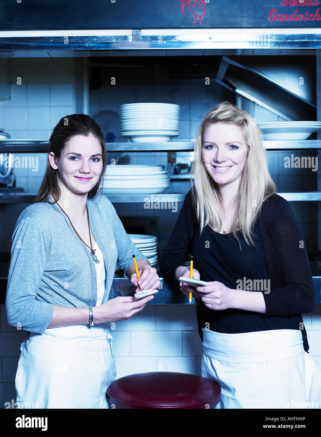 Two young waitresses holding notepads, smiling, portrait Stock Photo ...