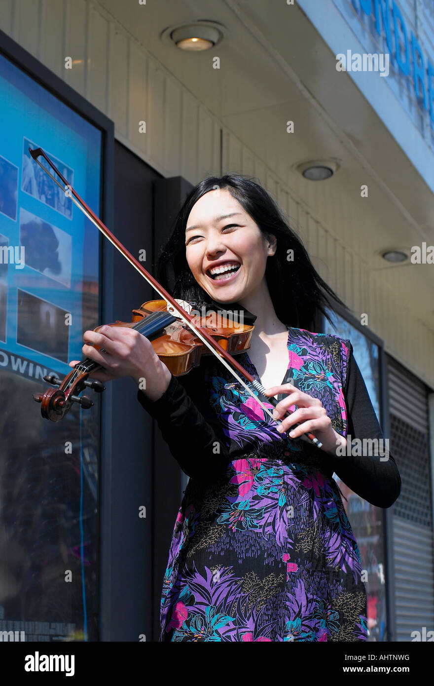 Young female busker playing violin outside cinema, smiling Stock Photo ...