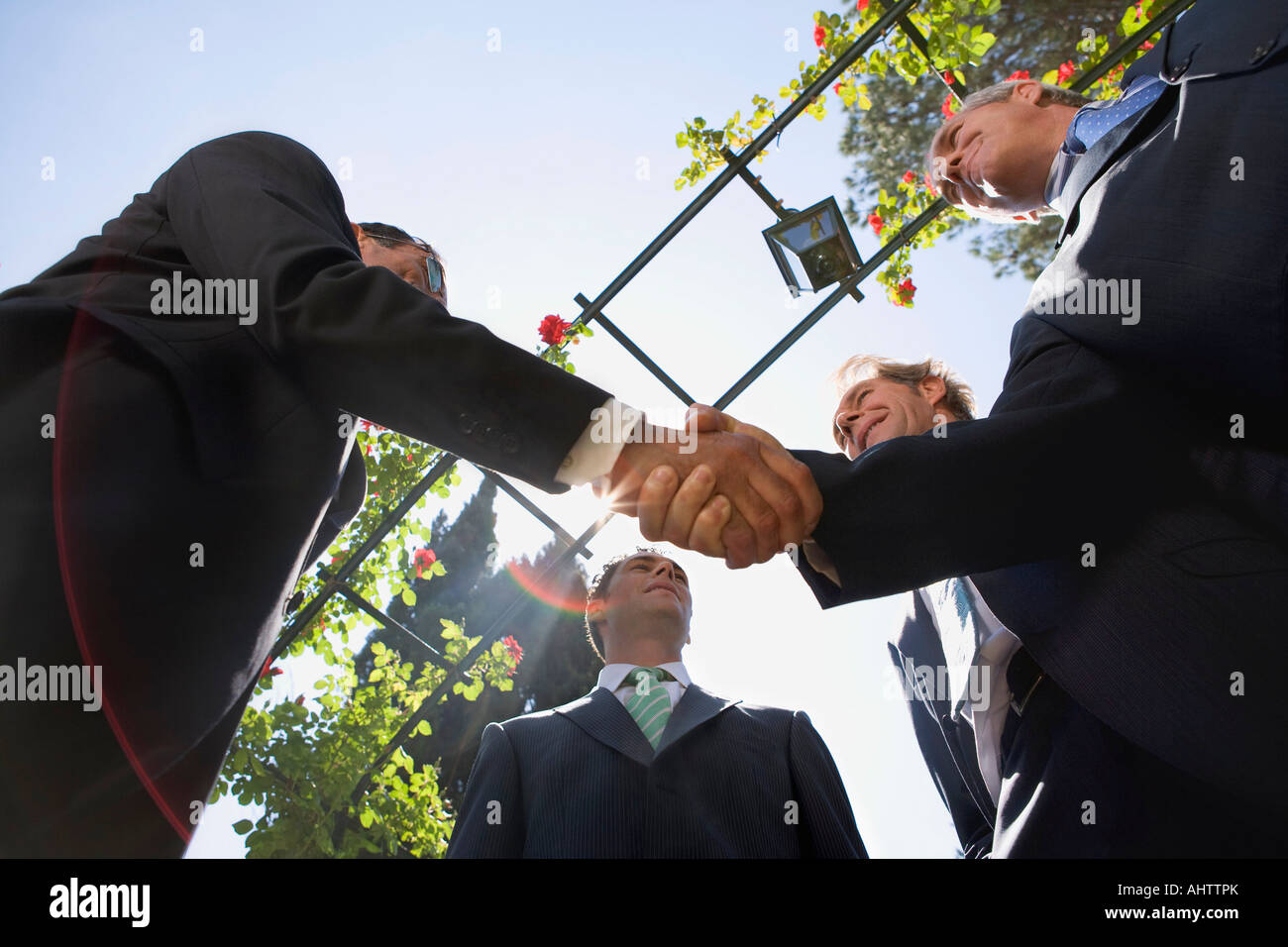 Four businessmen shaking hands in a garden Stock Photo - Alamy