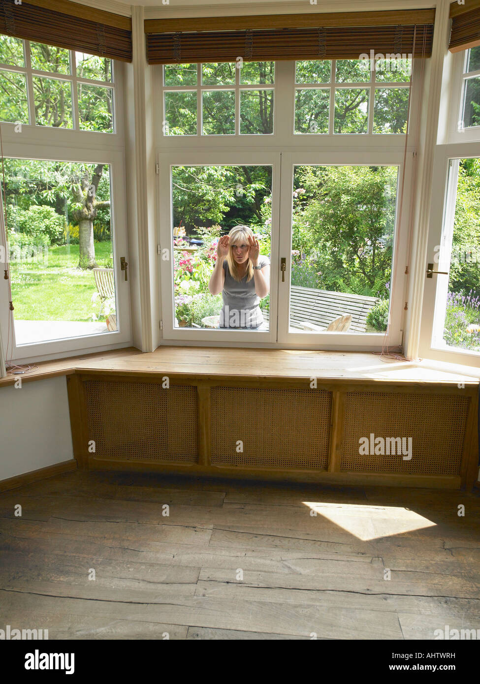 Blond woman looking through window into empty room Stock Photo - Alamy