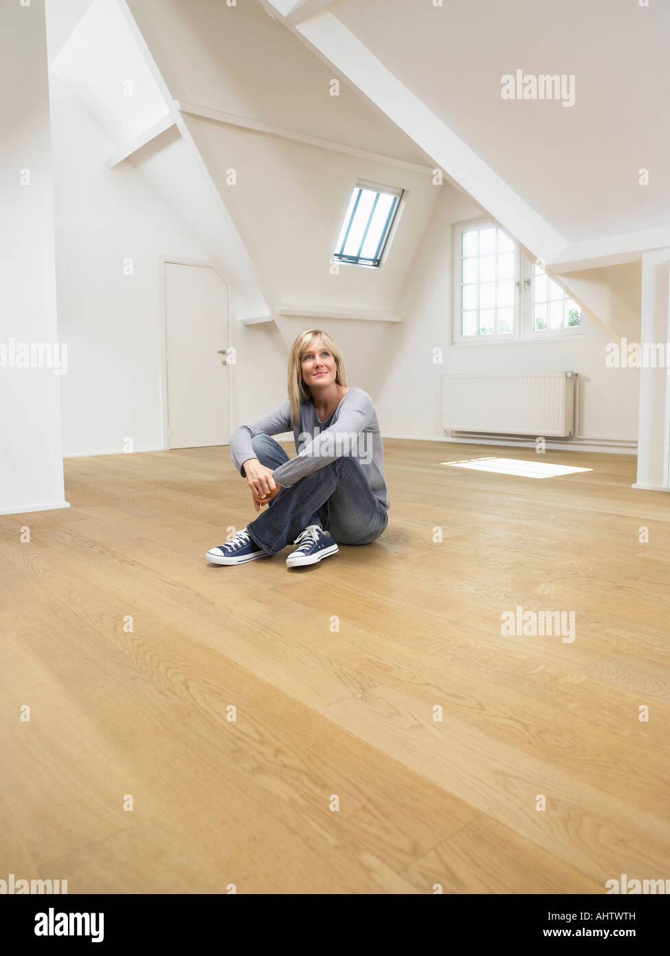 Woman seated on wooden floor of empty white loft Stock Photo - Alamy