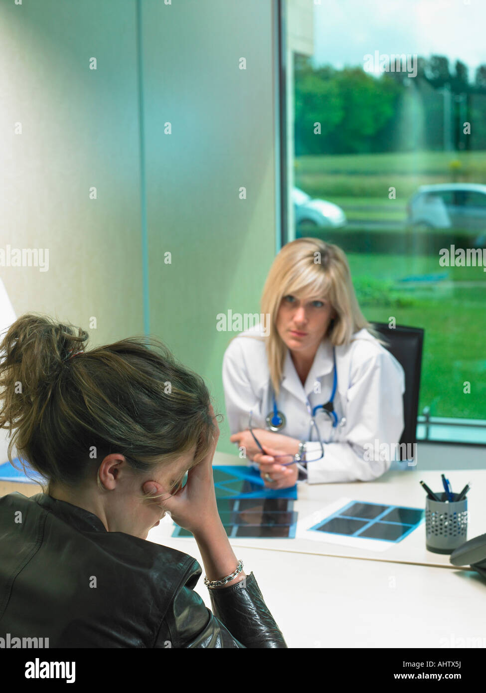 Concerned female doctor at her desk with stressed patient in foreground ...