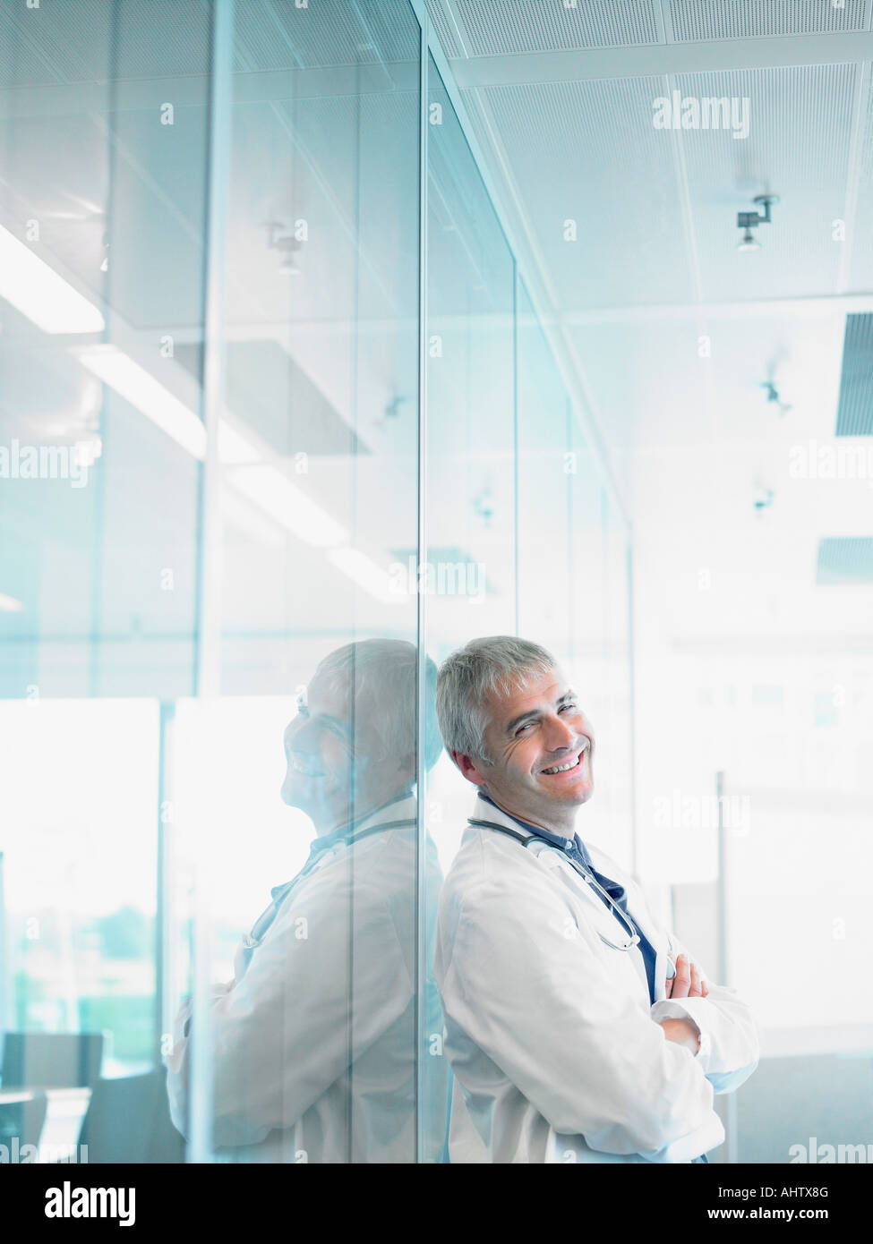 Smiling male doctor leaning on glass wall in hospital lobby Stock Photo ...