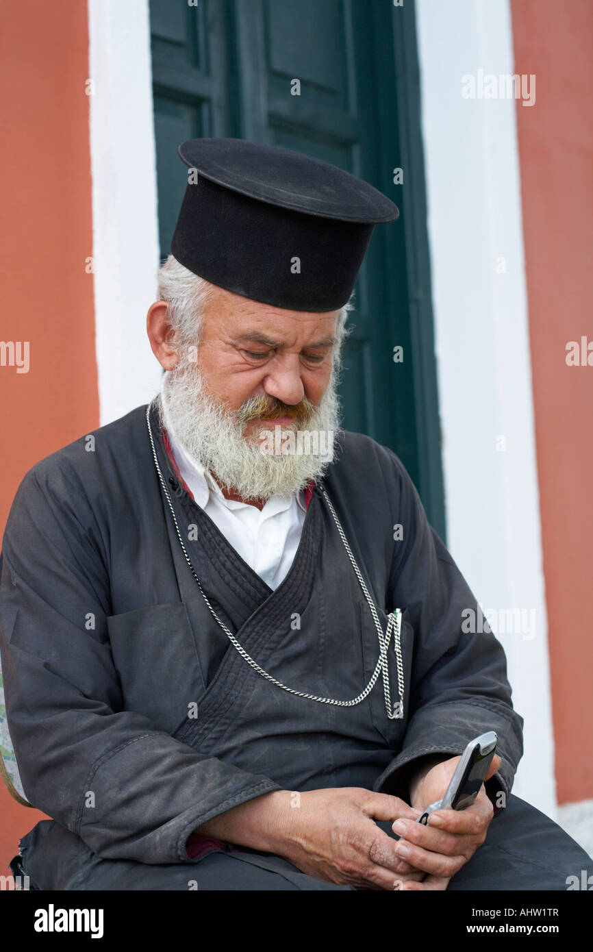 Old priest in front of church looking at display of his mobile Stock ...