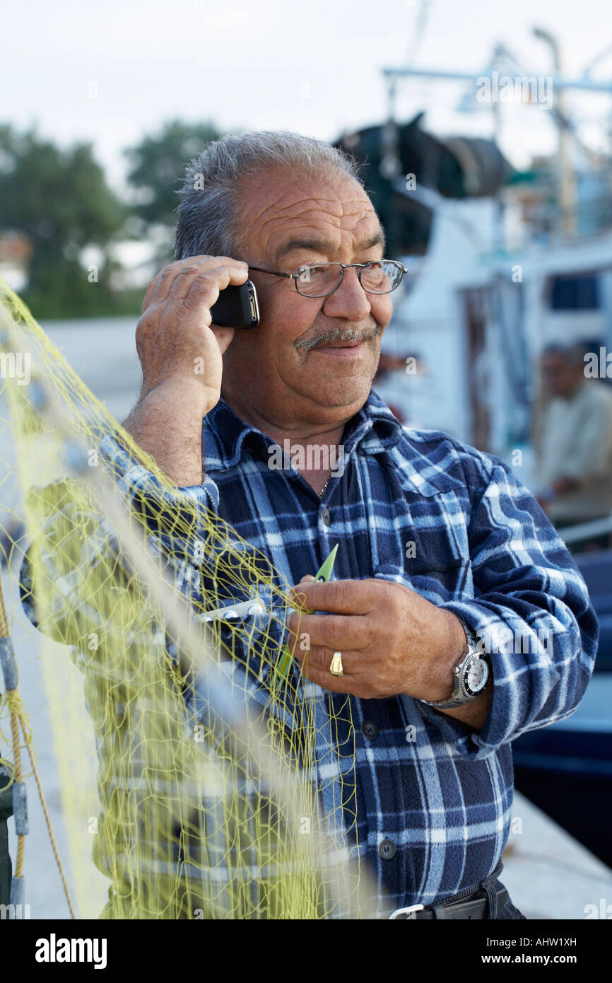 Mature fisherman fixing net while on cell phone Stock Photo - Alamy