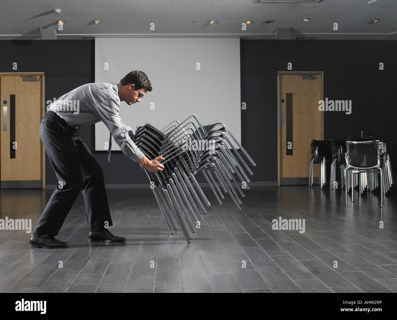 Man moving stack of chairs in empty presentation room Stock Photo - Alamy