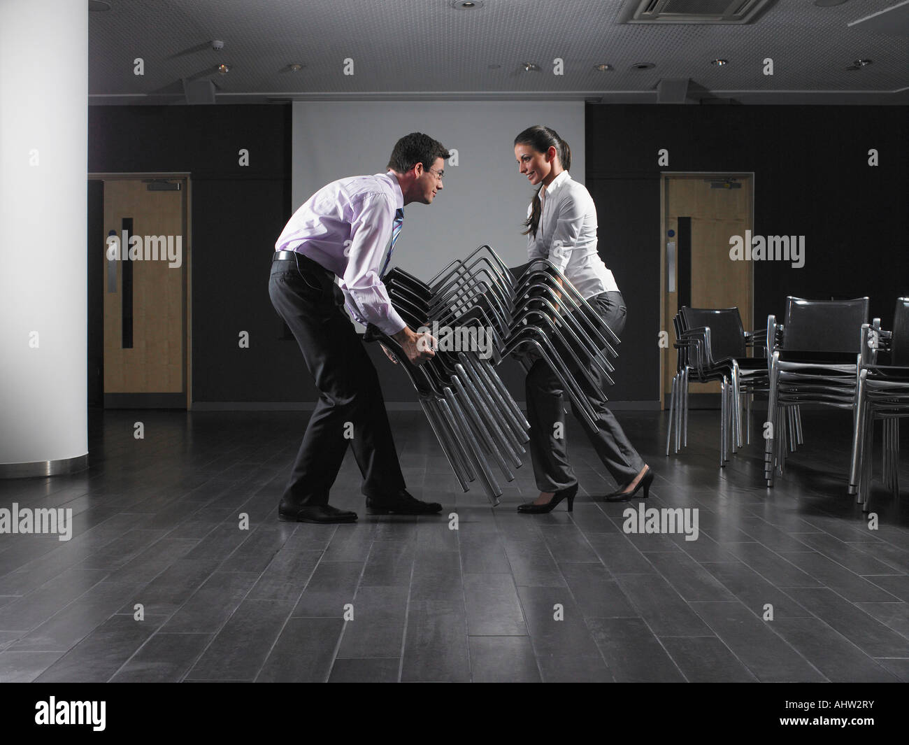 Man and woman moving stack of chairs in empty presentation room Stock ...