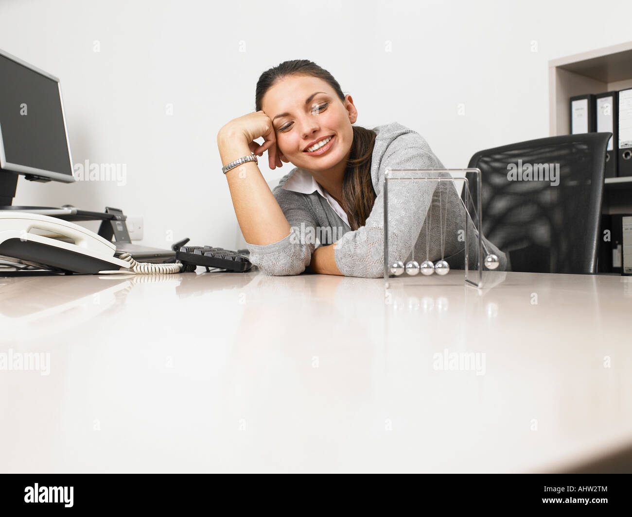 Businesswomen sitting at her desk with a Newton's Cradle Stock Photo ...