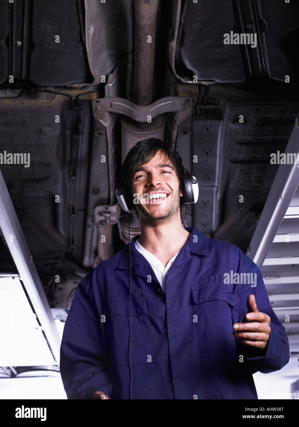 Mechanic standing under raised car listening to music Stock Photo - Alamy
