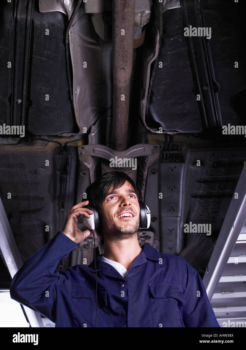 Mechanic standing under raised car listening to music Stock Photo - Alamy
